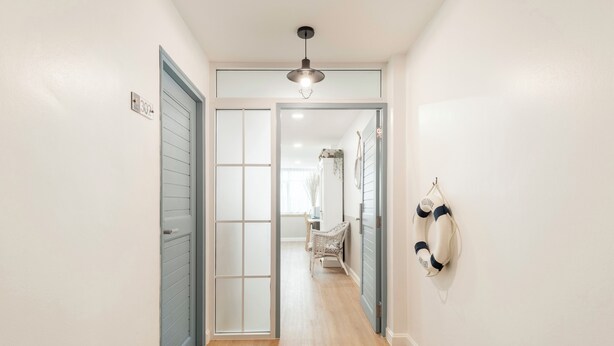 Um corredor com piso de madeira, uma porta com placa de número e um salva-vidas fixado na parede.