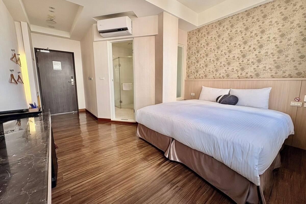 Quarto de hotel com uma cama grande, um closet espaçoso, chuveiro e bancada de mármore.