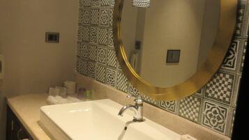 Uma casa de banho com uma pia branca, um espelho com moldura dourada, azulejos de padrão decorativo e duas luzes fixadas na parede.