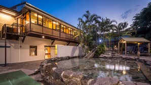Um edifício moderno com varanda com vista para uma área de piscina, rodeado por plantas tropicais.