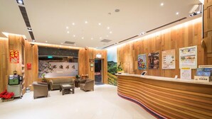 Uma área de recepção de hotel com um balcão de madeira, sala de estar e um pôster grande na parede.