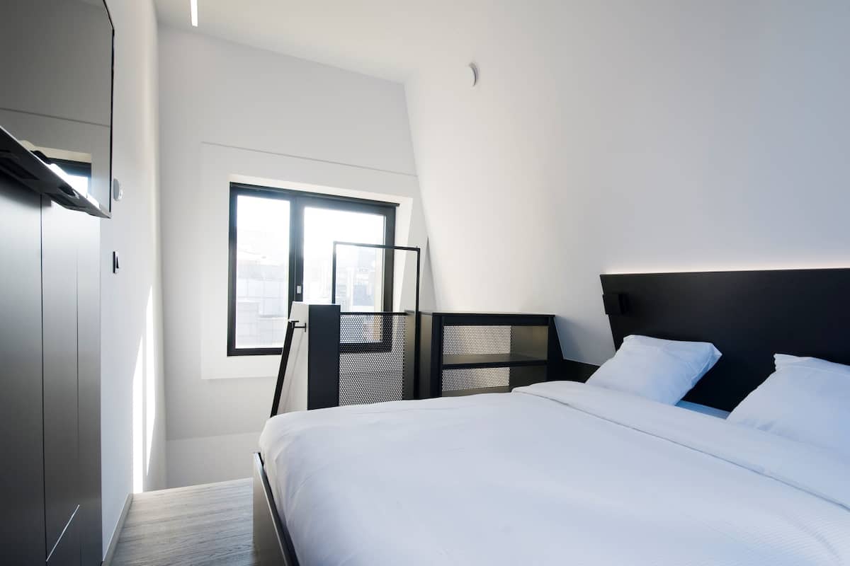 Quarto de hotel moderno com uma cama grande, um guarda-roupa e uma janela com vista para a cidade.