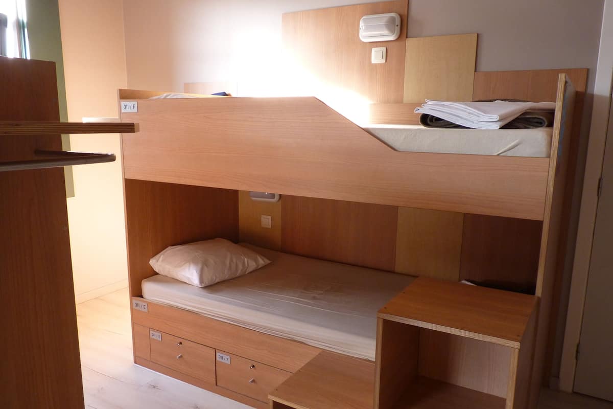 Uma cama beliche com escrivaninha e gavetas, um interruptor de luz e um espelho na cabeceira.