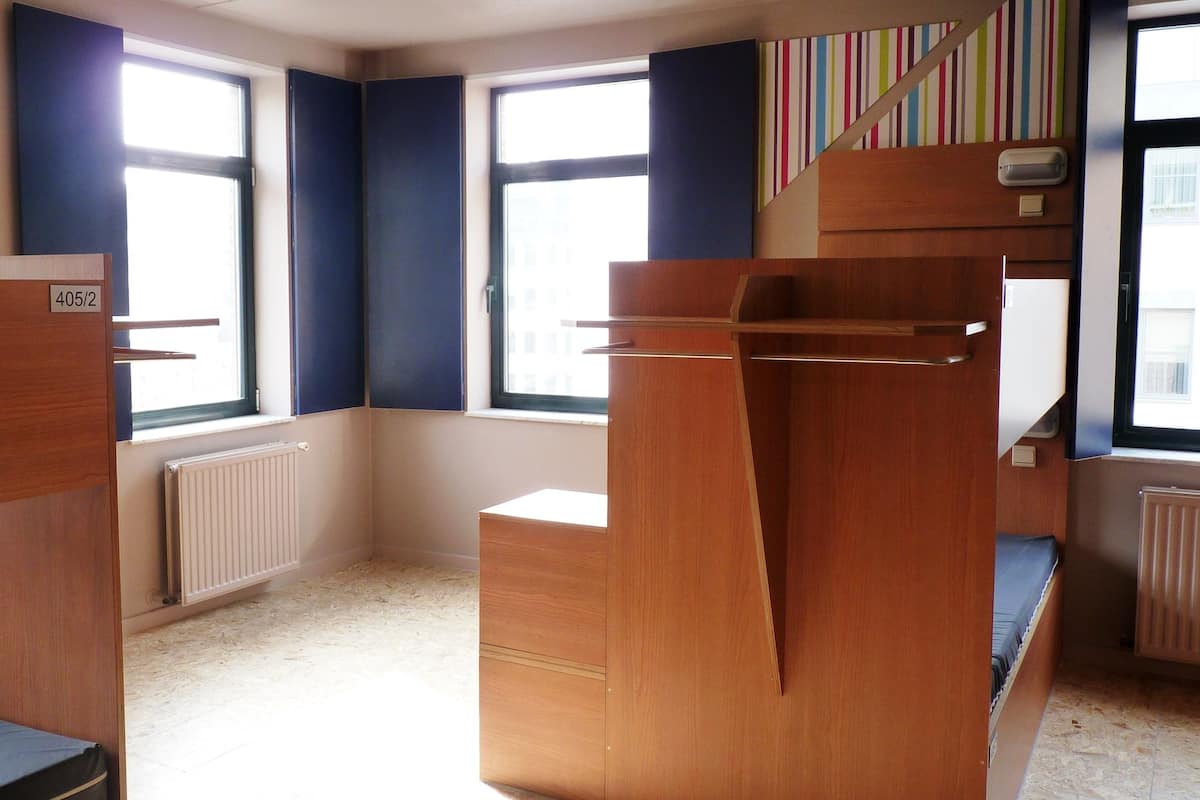 Quarto com beliches, radiador e janelas amplas com cortinas listradas.