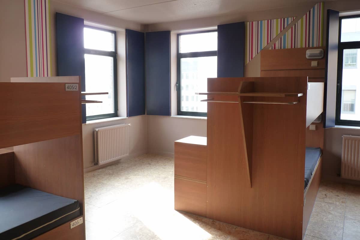 Quarto de dormitório com beliches, radiador e janelas amplas.