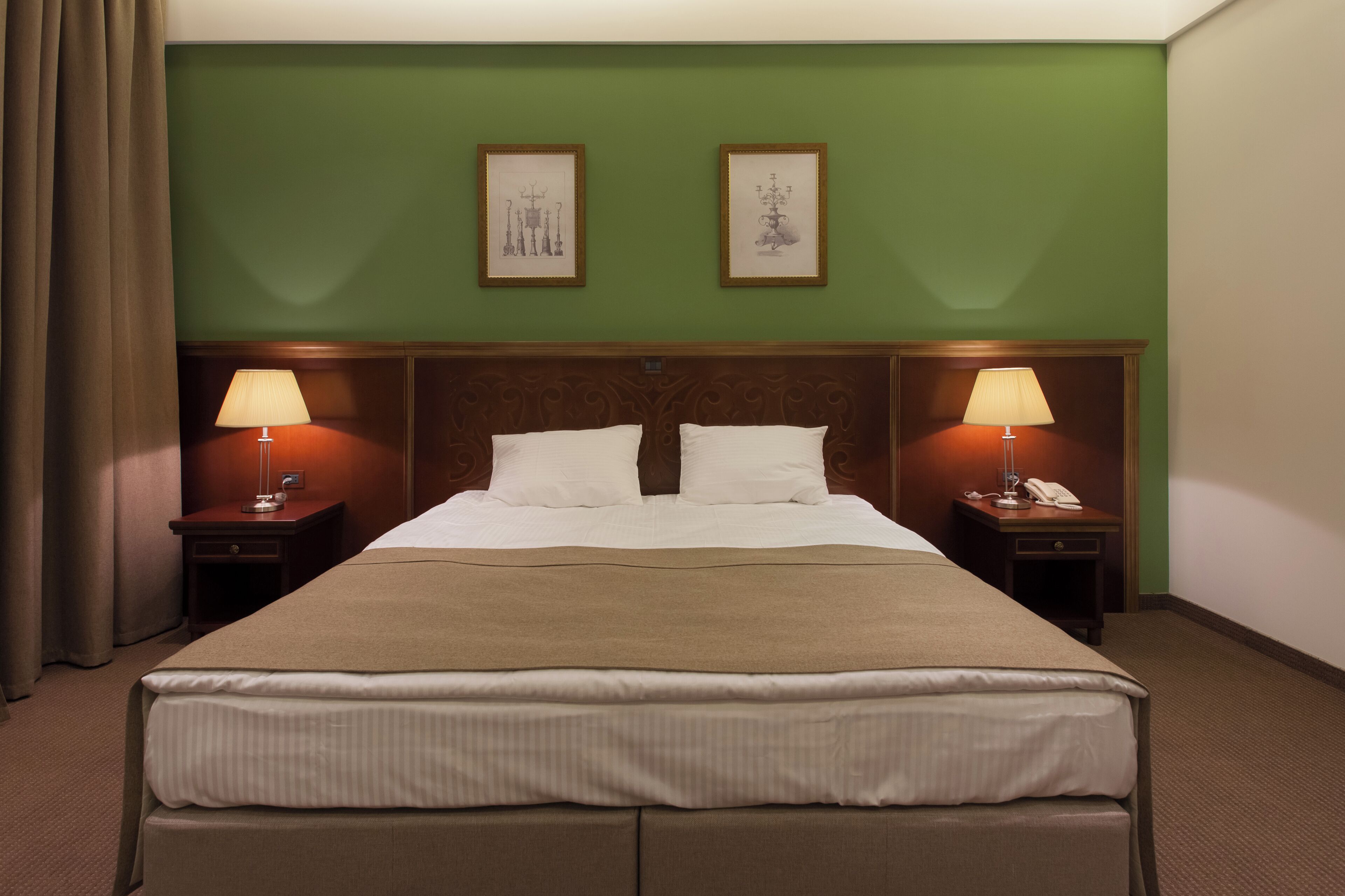 Quarto de hotel com uma cama grande, duas mesas de cabeceira com luminárias e duas imagens emolduradas na parede.