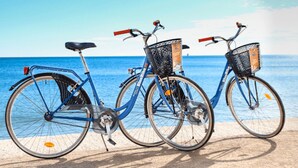Duas bicicletas estacionadas numa praia de areia, com o oceano ao fundo.