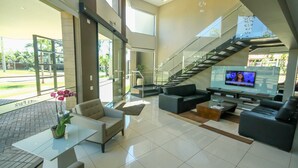Uma sala de estar espaçosa com design moderno, com uma televisão de tela plana grande, assentos confortáveis e uma escada que leva a um andar superior.