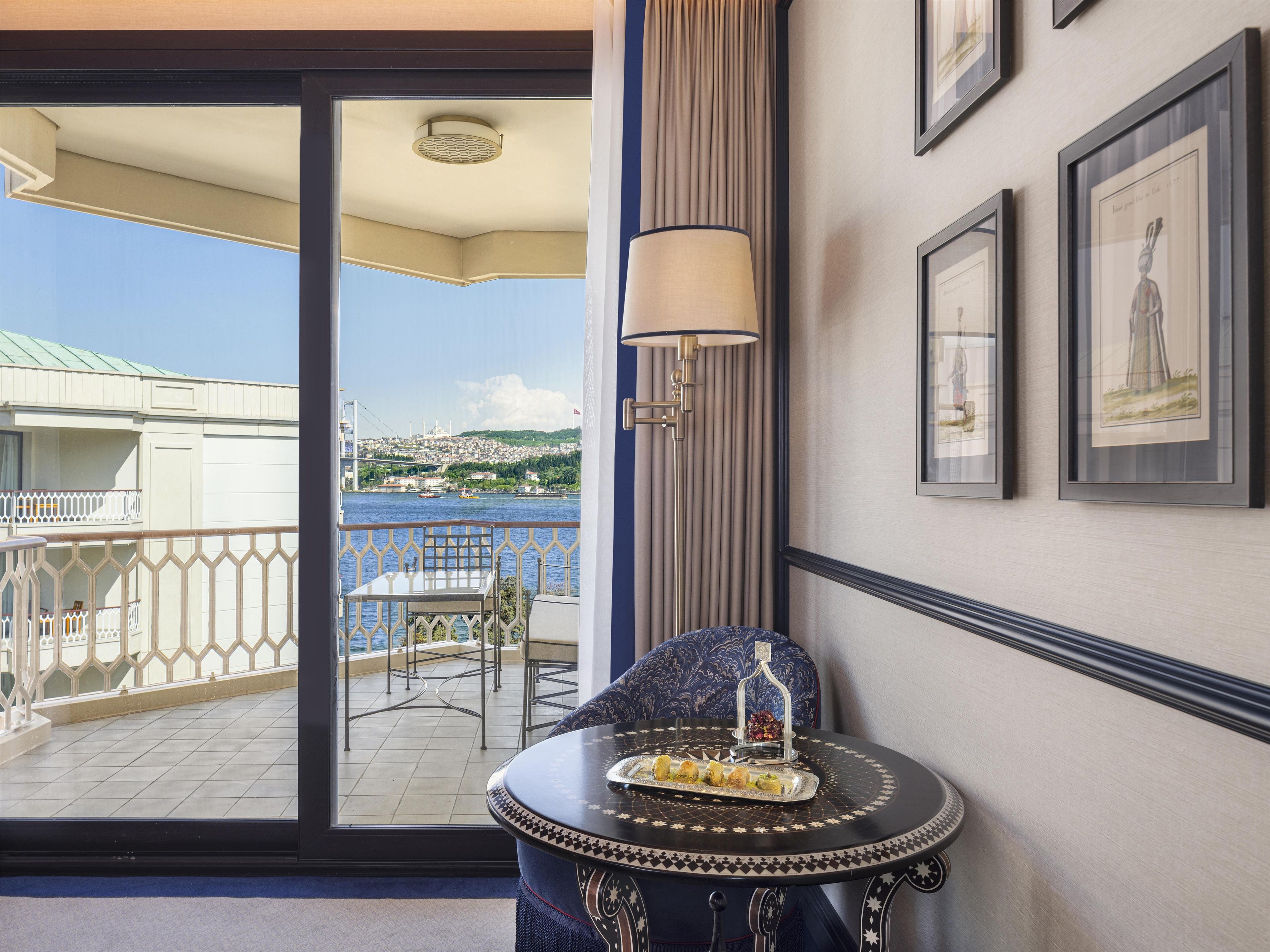 Quarto de hotel com varanda, uma mesa com bandeja de doces e quadros nas paredes.