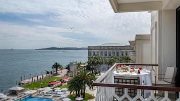 Varanda com mesa posta para refeições, com vista para uma piscina e o litoral.