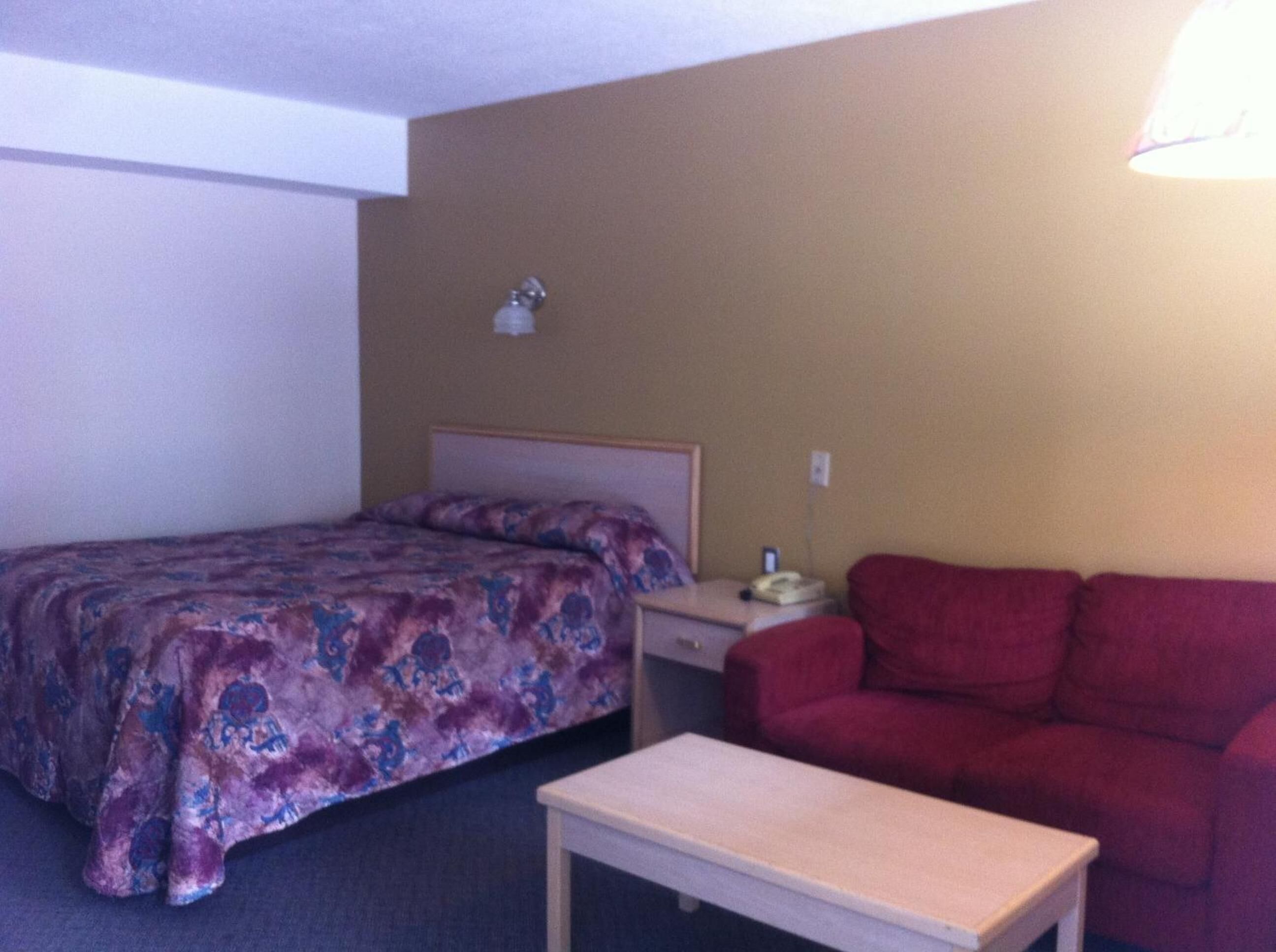 Quarto de hotel com cama, sofá vermelho, mesa pequena e criado-mudo com telefone.