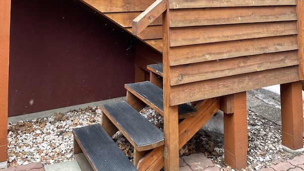 Uma cabana de madeira com uma escadaria que leva a uma porta com janela em arco.