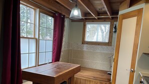 Uma cozinha compacta com mesa de madeira, janela com cortinas, pia embutida e uma porta.