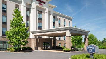 Um hotel Hampton Inn com entrada desobstruída, sinal indicando altura livre de 3,8 metros e uma placa de boas-vindas.