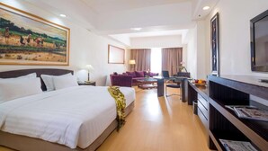 Quarto de hotel com uma cama grande, uma escrivaninha com computador, televisão e um quadro na parede.