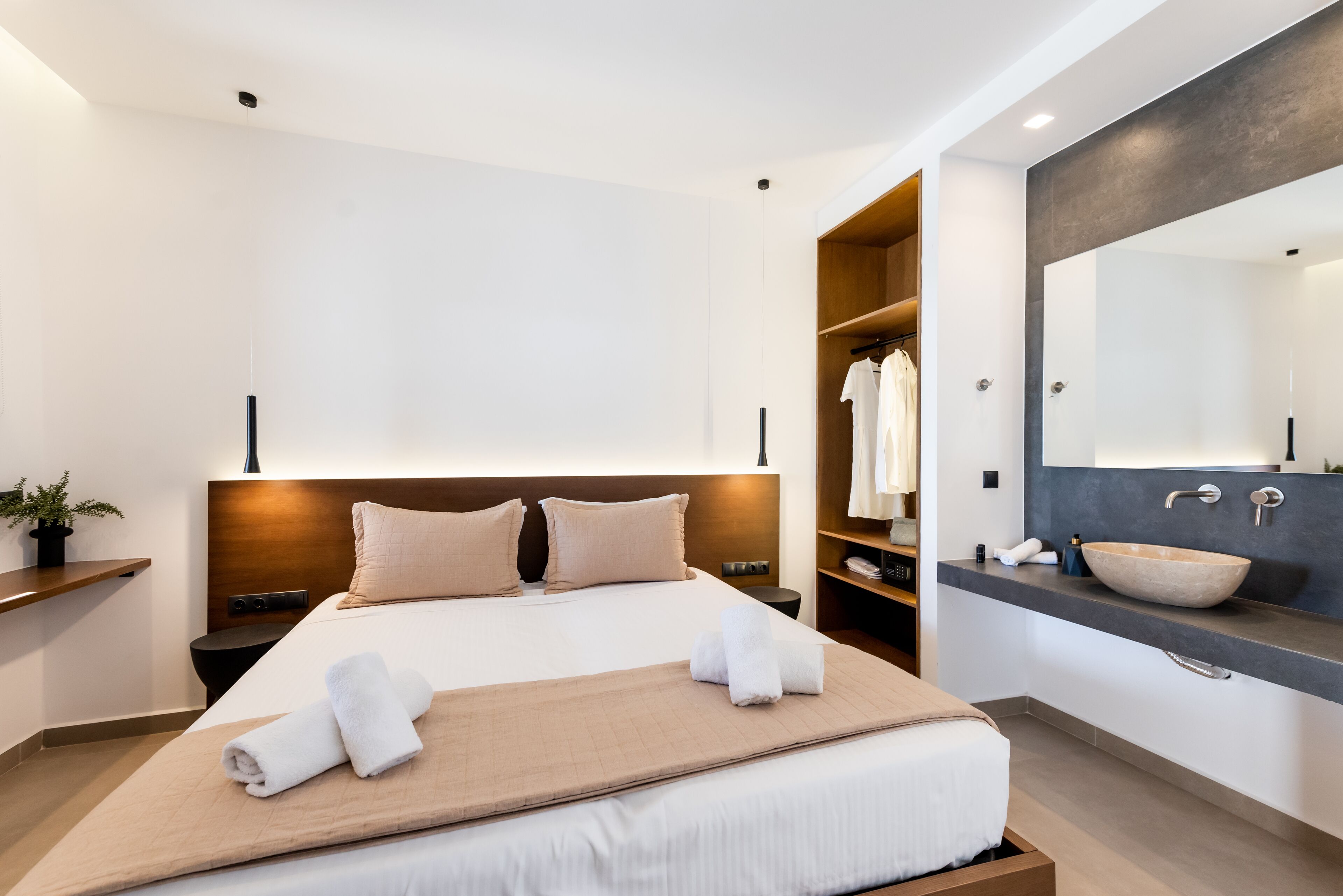 Quarto de hotel moderno com uma cama grande, mesa de cabeceira, armário embutido, penteadeira com um espelho grande e uma janela ampla.