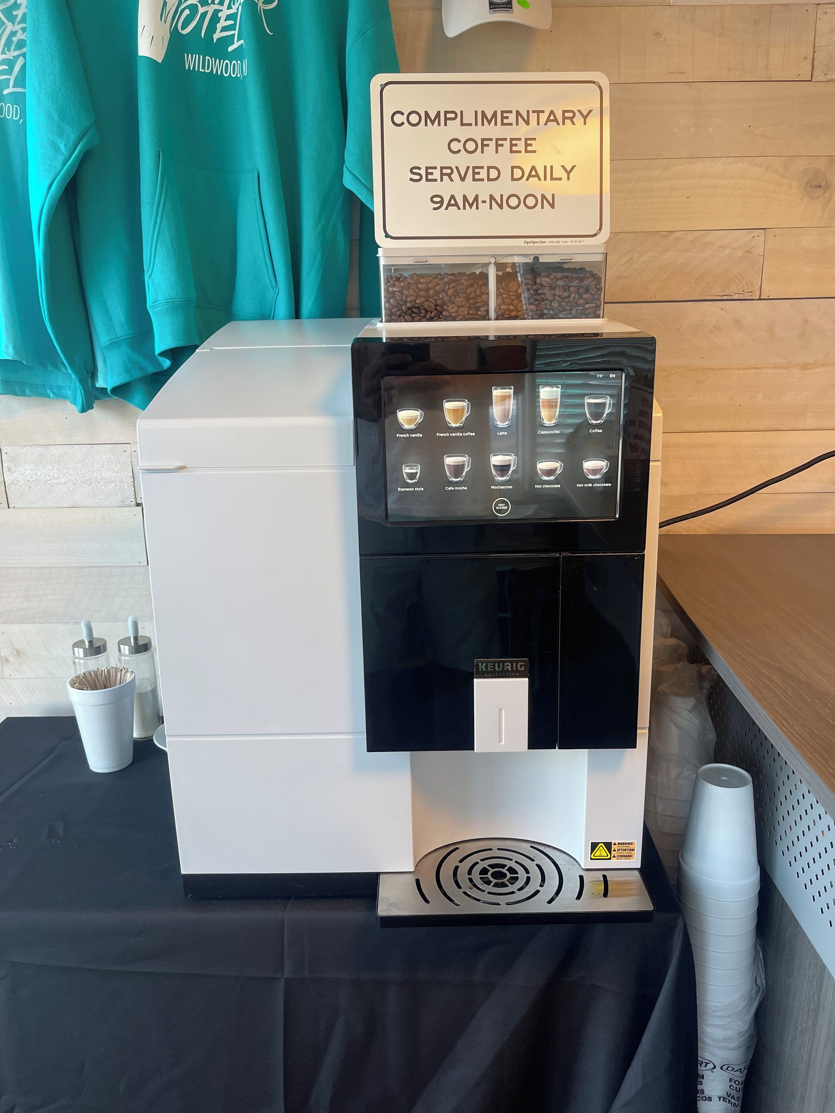 Máquina de café com aviso indicando café cortesia servido diariamente das 9h ao meio-dia.