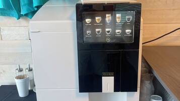 Máquina de café com aviso indicando café cortesia servido diariamente das 9h ao meio-dia.