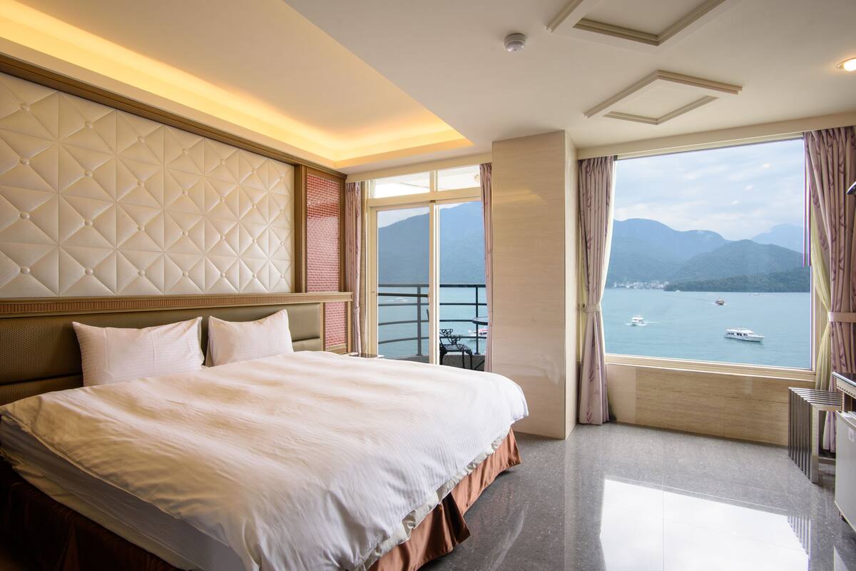 Quarto de hotel com uma cama grande, vista para o mar e varanda com guarda-corpo.