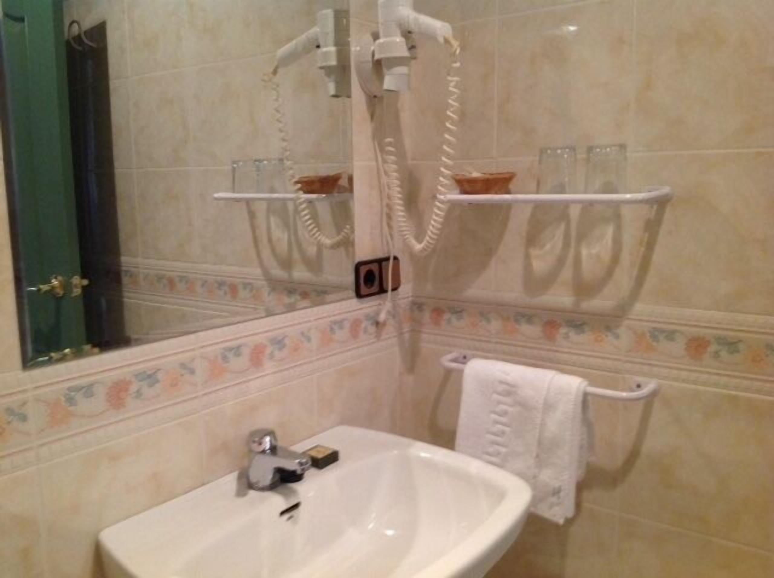Casa de banho com lavatório, espelho, porta-toalhas e um secador de cabelo numa prateleira.