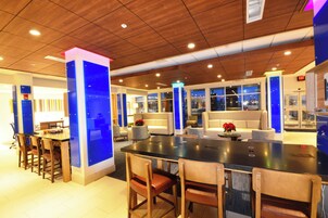 Um hall de hotel moderno com área de bar central, opções de assento e vista através de grandes janelas.