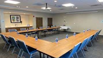 Uma sala de conferências com uma mesa comprida, cadeiras, garrafas de água, um projetor e um quadro branco.