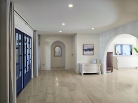 Um corredor amplo com piso de mármore, um aparador branco, uma obra de arte emoldurada e uma televisão em um móvel.
