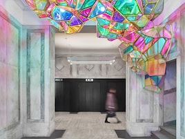 Um hall com um lustre moderno, paredes de mármore e área de elevadores.