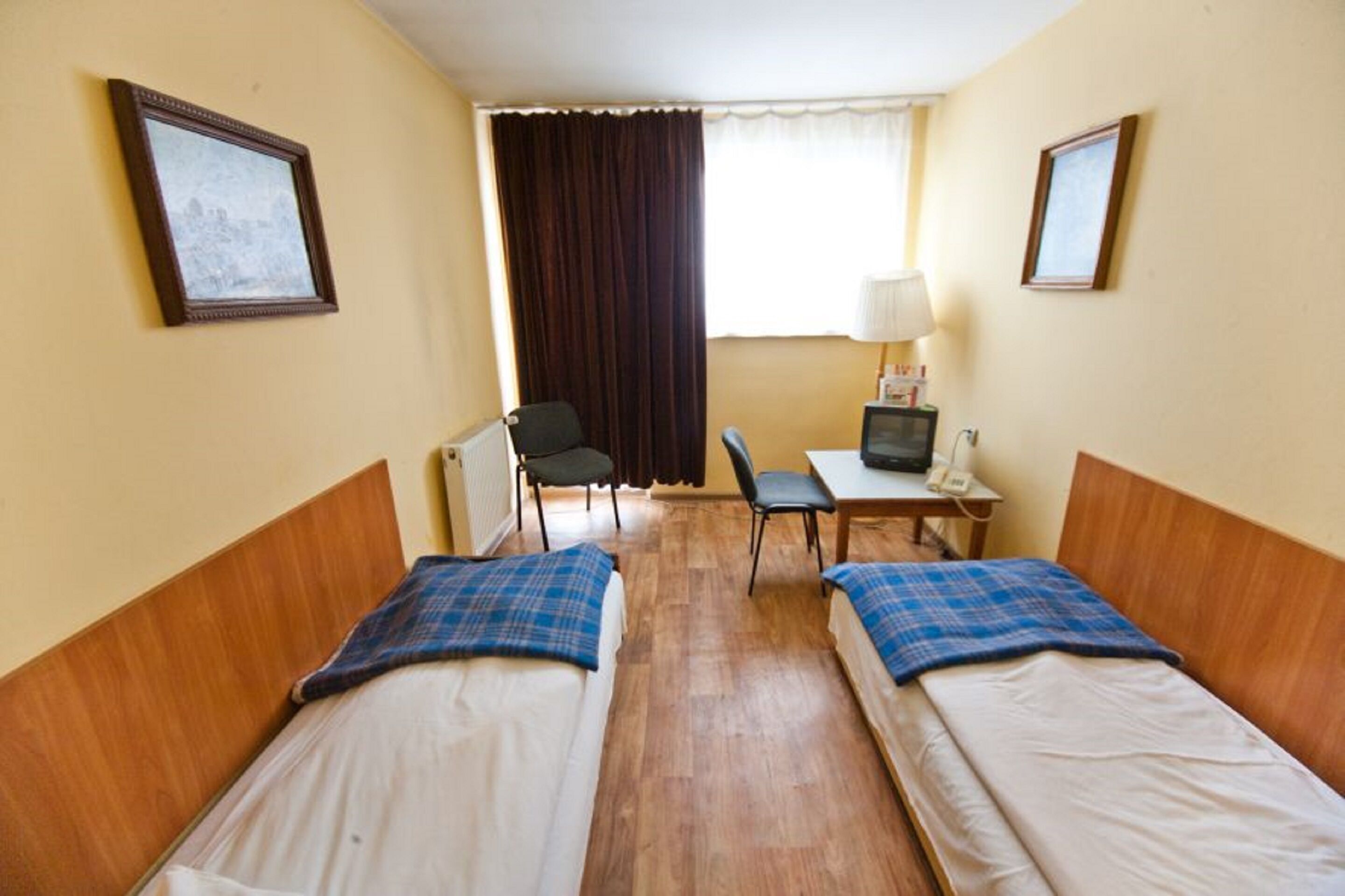 Quarto de hotel com duas camas de solteiro, uma escrivaninha com cadeira, televisão e janela com cortinas.