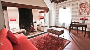 Uma sala de estar acolhedora com lareira, sofá vermelho, tapete estampado e um espaço de jantar com mesa e cadeiras.