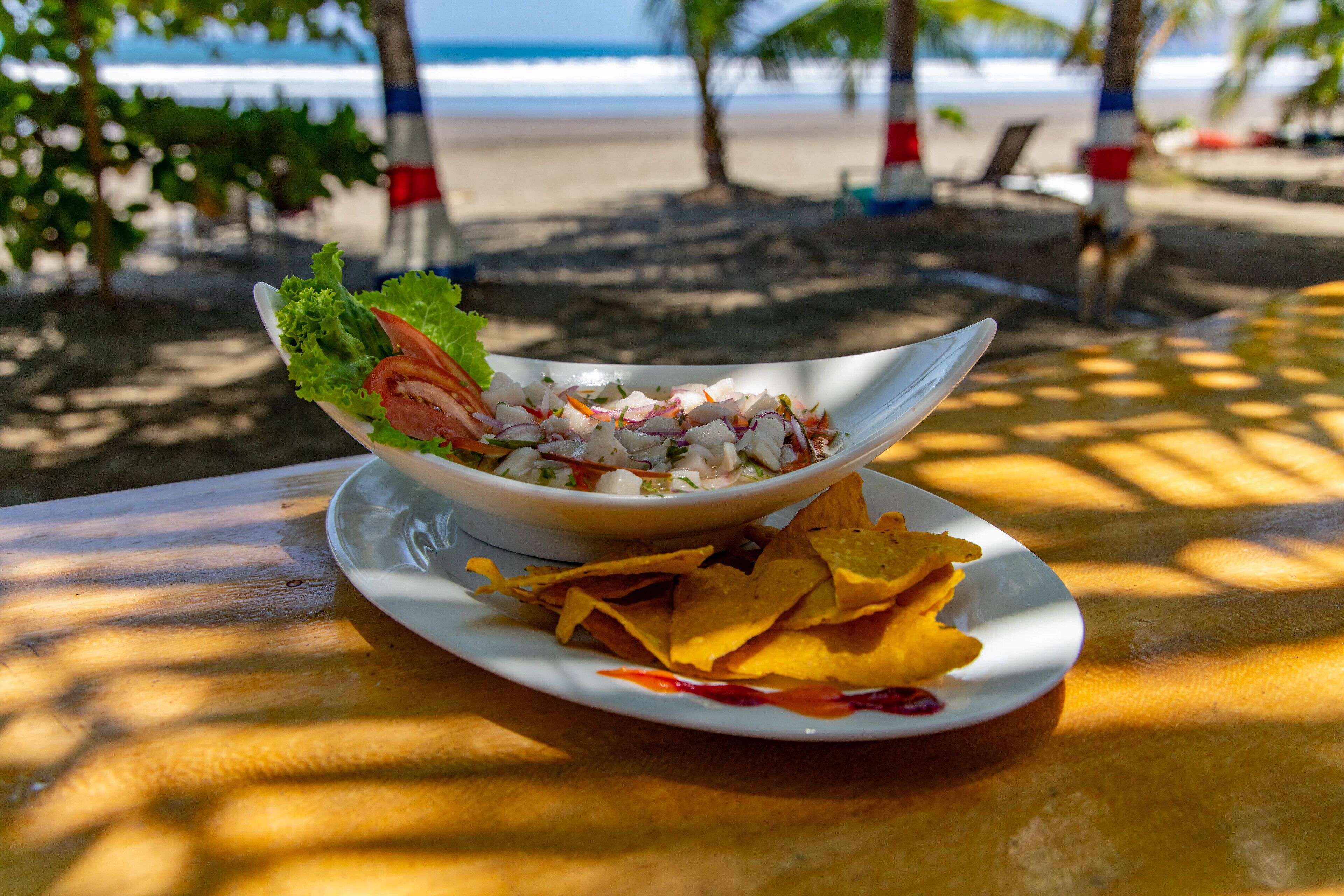 Uma salada de mariscos e tortilhas com queijo numa mesa, com vista para a praia ao fundo.