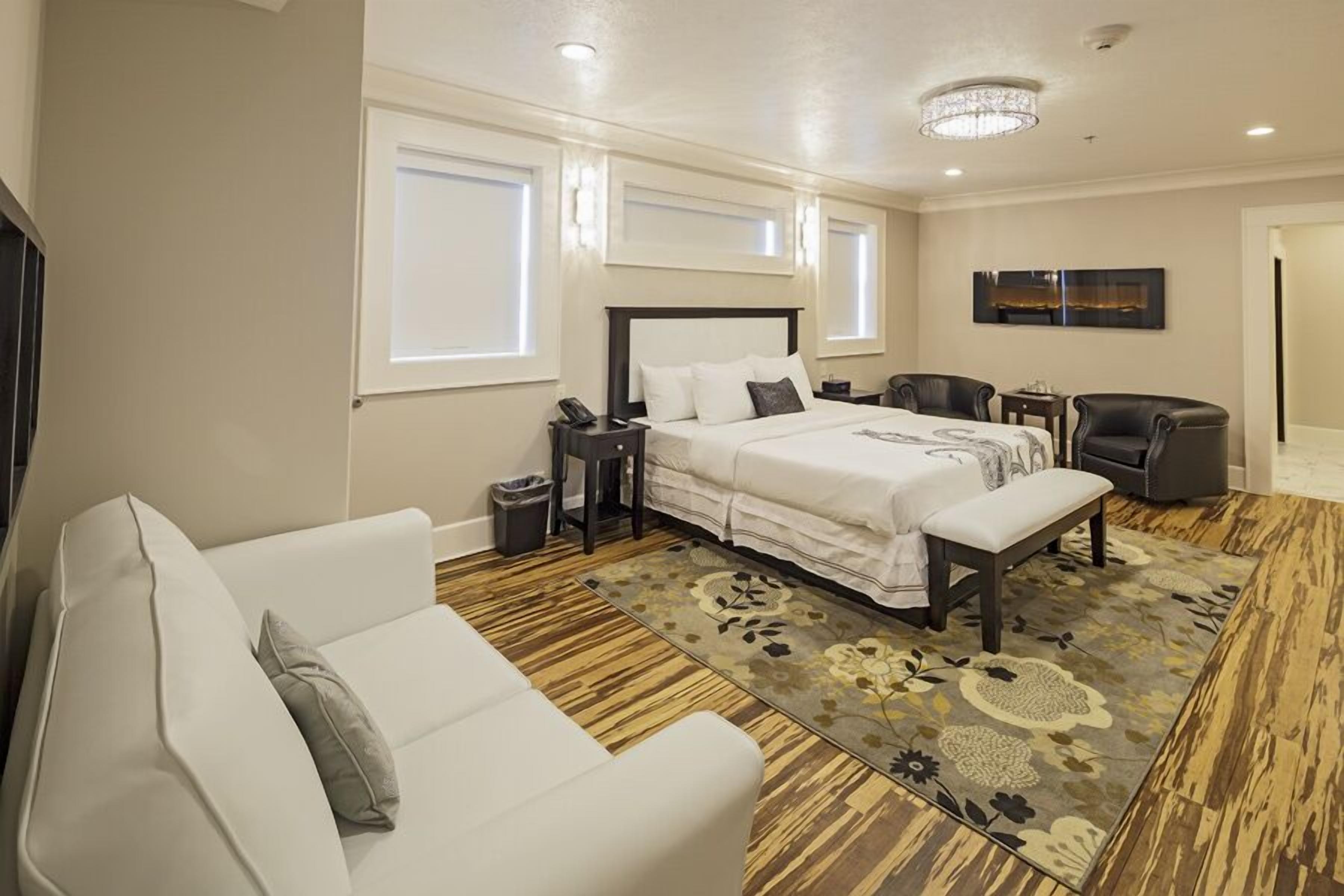 Quarto de hotel moderno com uma cama grande, um sofá, duas poltronas, uma mesinha e um candelabro.