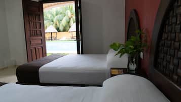 Quarto de hotel com duas camas, porta de madeira, vista para piscina e palmeiras, e um vaso de planta.