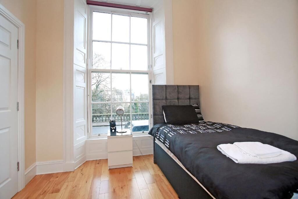 Quarto com cama, janela, mesa de cabeceira e porta.