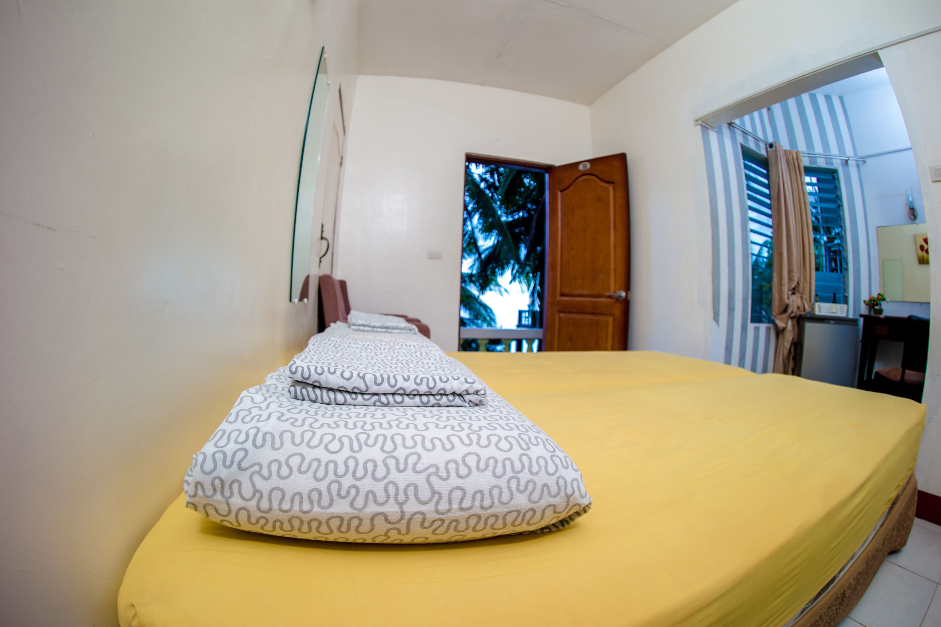Uma cama de solteiro com um edredom estampado, uma janela com cortinas e uma porta que dá para o exterior.