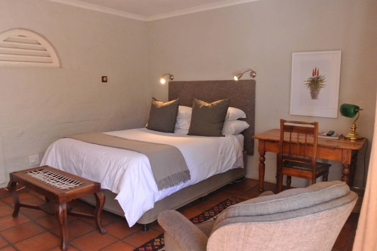 Um quarto com cama, mesa de cabeceira, cadeira e escrivaninha com cadeira.