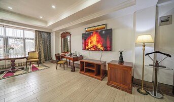 Uma sala de estar bem iluminada com lareira, televisão, escrivaninha e abajur.
