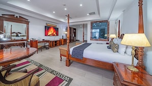Quarto de hotel com cama de dossel, escrivaninha com cadeira, televisão e lareira.