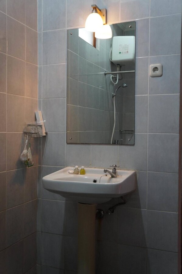 Casa de banho com lavatório branco, espelho e candeeiro fixado na parede.