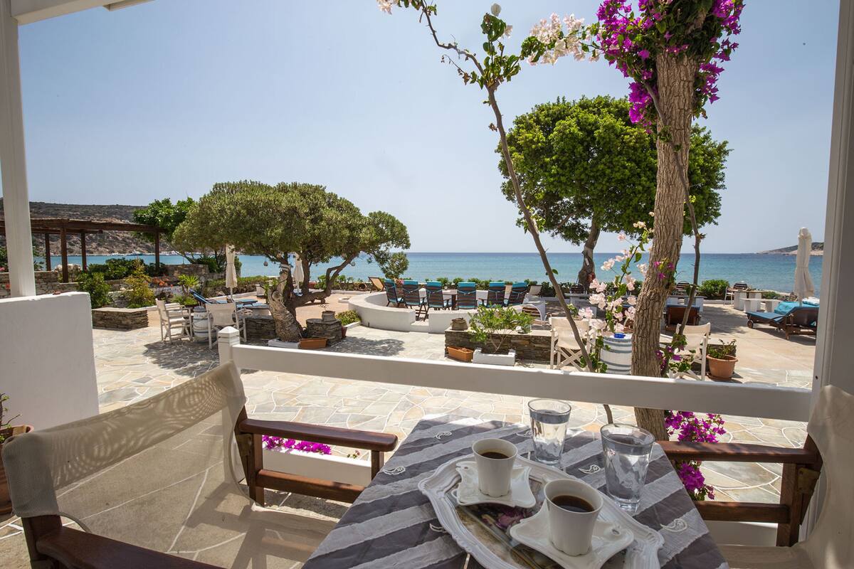 Um terraço com mesas ao ar livre, uma mesa com bebidas e vista para o mar.