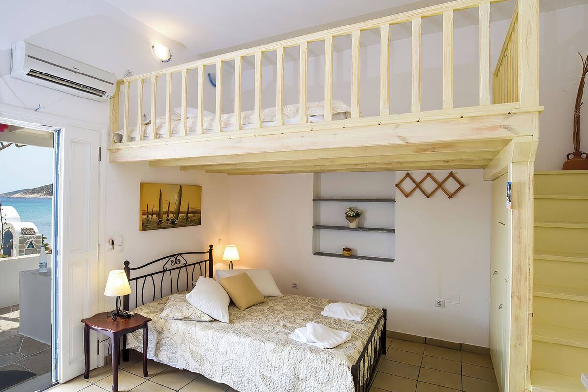 Quarto com beliche, mesa de cabeceira com luminária, um quadro e vista para o mar.