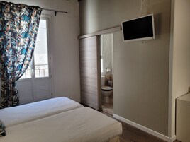Quarto com cama, televisão fixada na parede e banheiro visível por uma porta aberta.