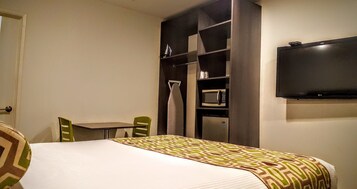 Quarto de hotel com cama, mesa pequena, cadeira, guarda-roupa, micro-ondas e televisão.