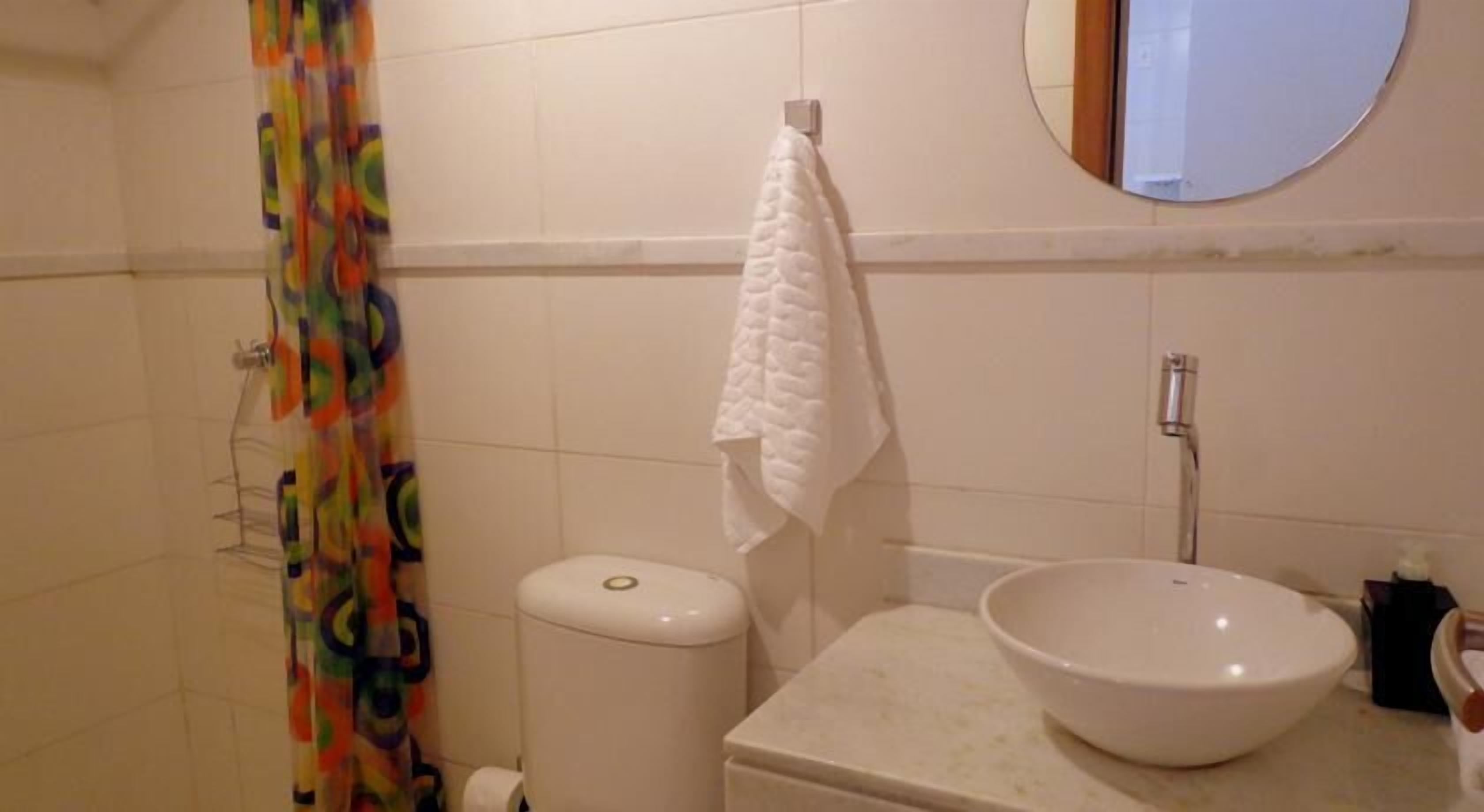 Casa de banho com sanita branca, lavatório branco e cortina de chuveiro colorida.