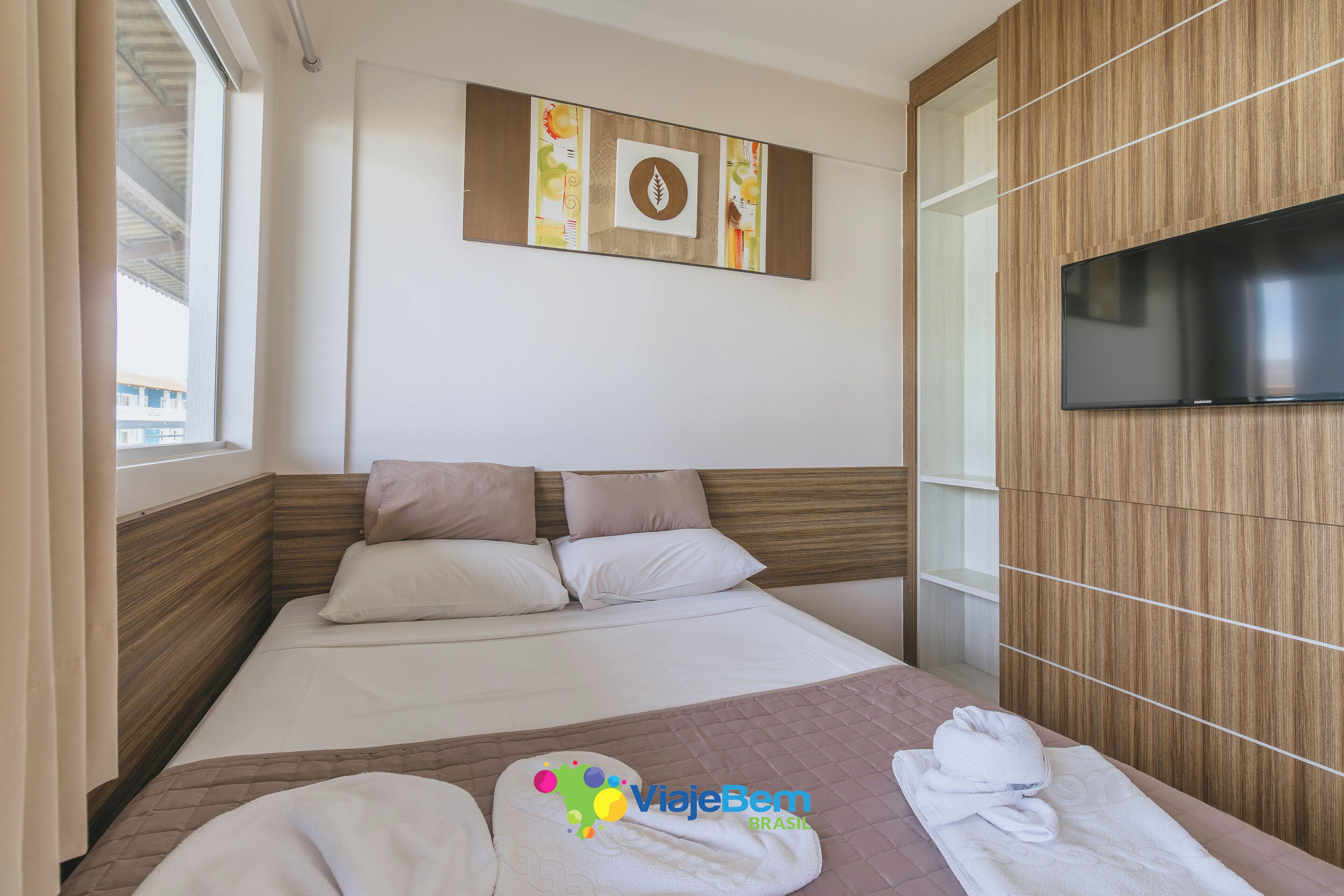 Quarto de hotel com uma cama, televisão na parede e uma janela.