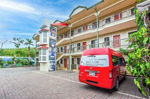Um hotel com vários andares, com uma carrinha vermelha estacionada em frente, uma escadaria e um mural na fachada.