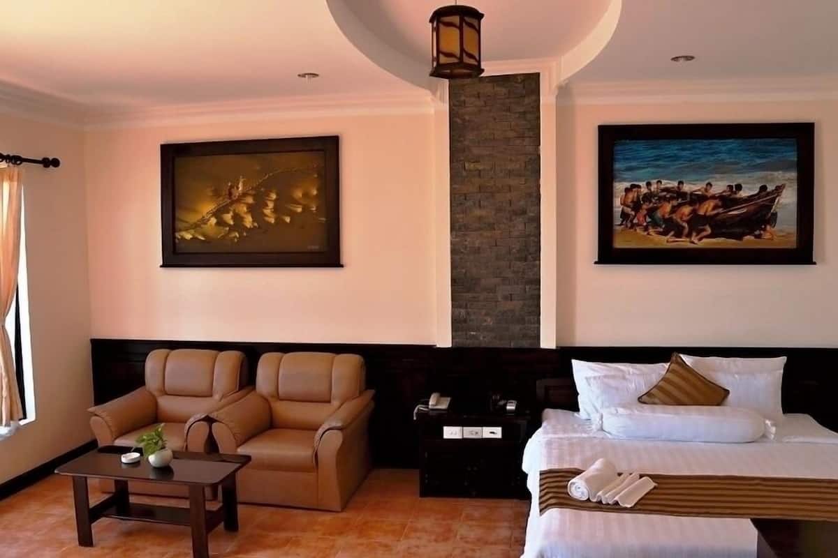 Quarto de hotel com cama, sofá, mesa de centro e duas pinturas nas paredes.