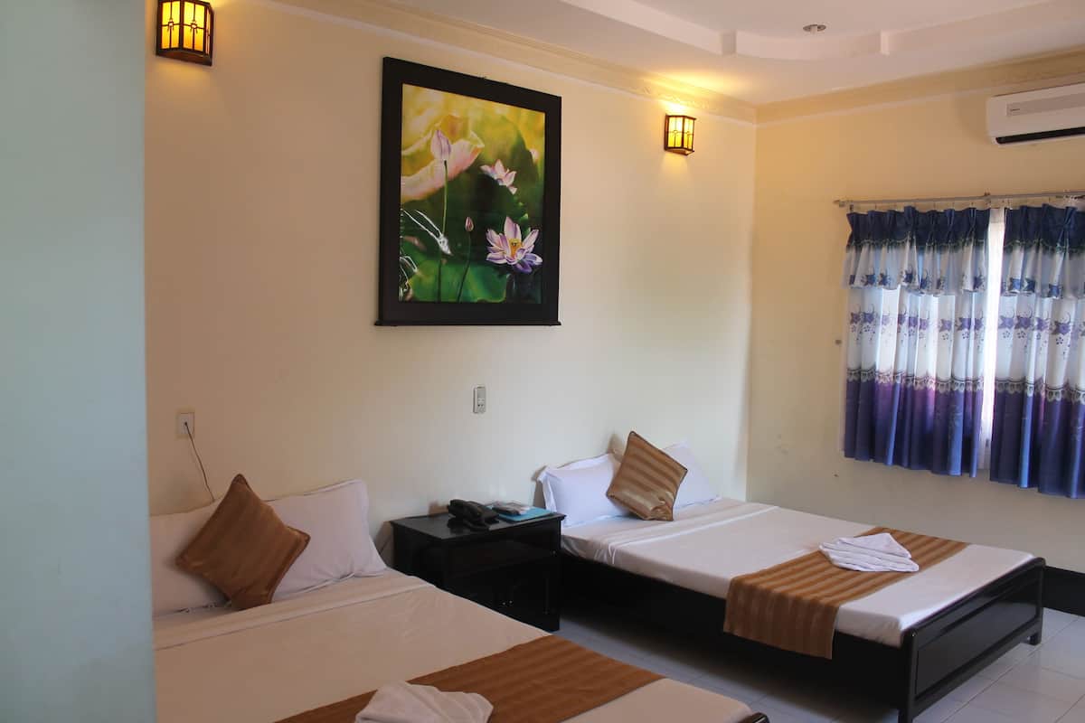Quarto de hotel com duas camas, um quadro de flores na parede e uma janela com cortinas.