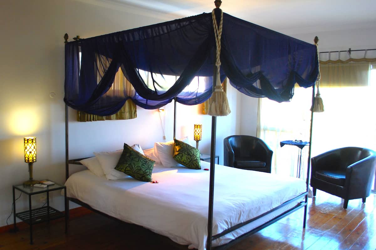Uma cama de dossel com cortina, uma mesinha de cabeceira, uma cadeira e um abajur.