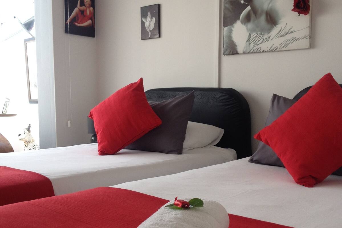 Quarto de hotel com duas camas, roupa de cama vermelha e branca, um cobertor vermelho e um quadro na parede.